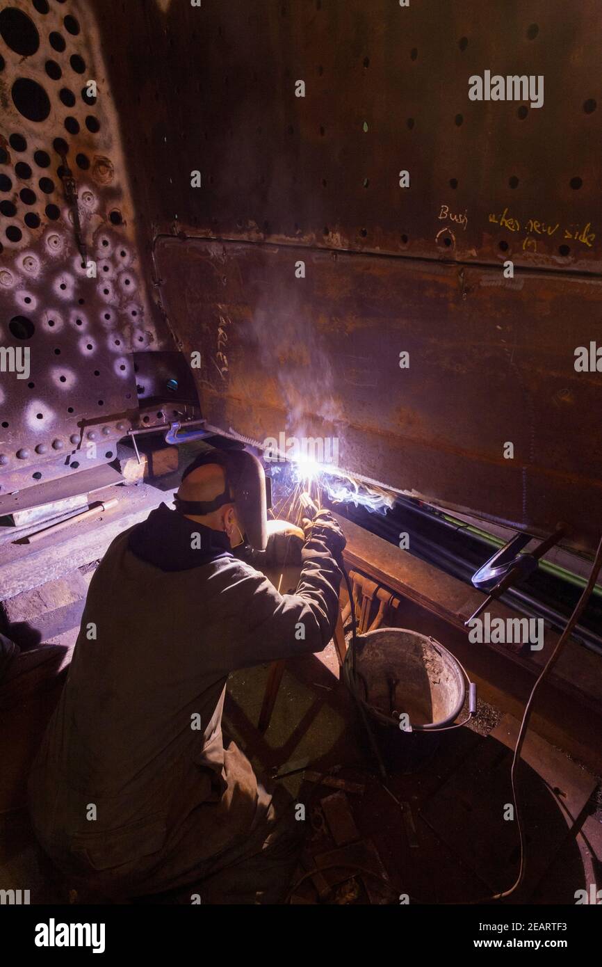 A welder working on the overhaul of an old steam locomotive in the workshop of the Keighley and ...