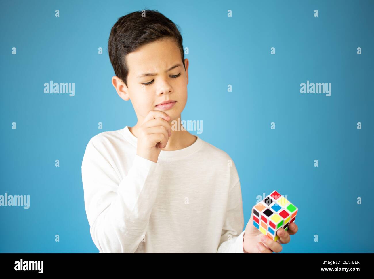 Young boy pensive plays with rubik's cube over blue background Stock ...