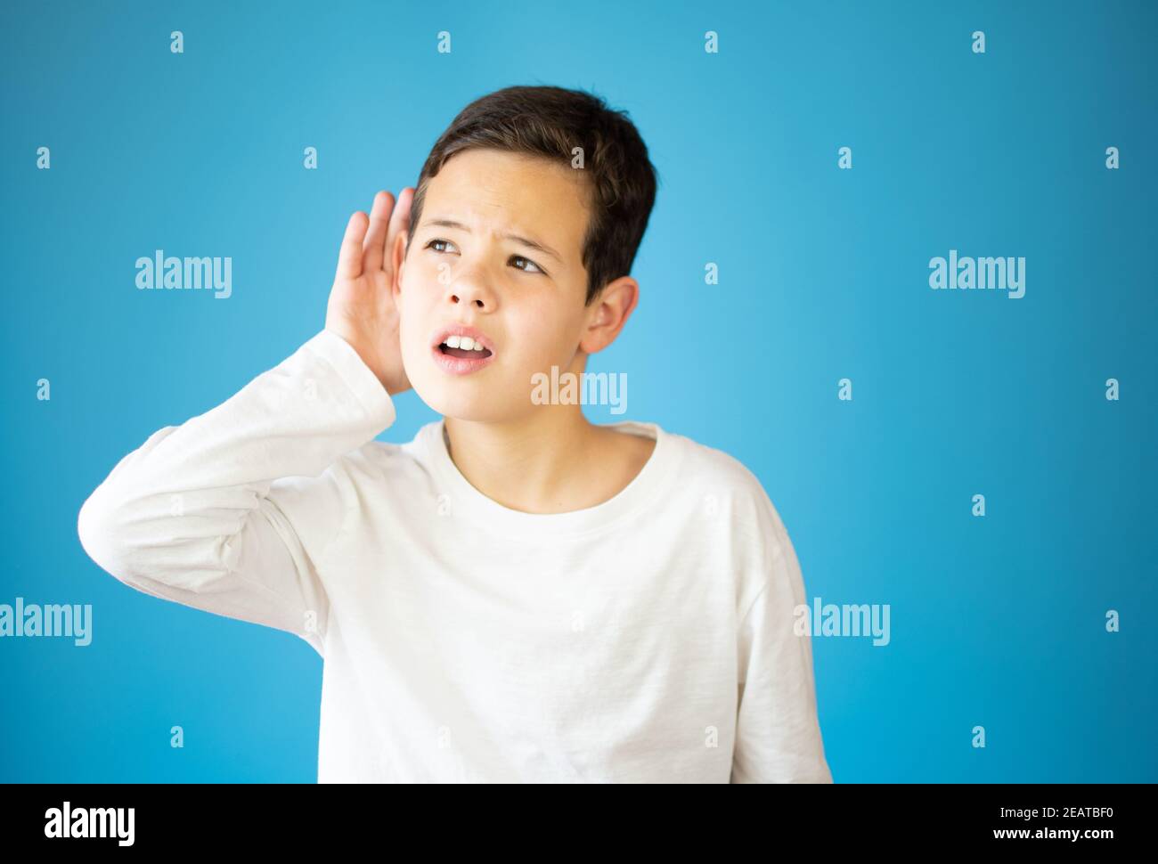 Concentrated young boy making a gesture of trying to hear something ...