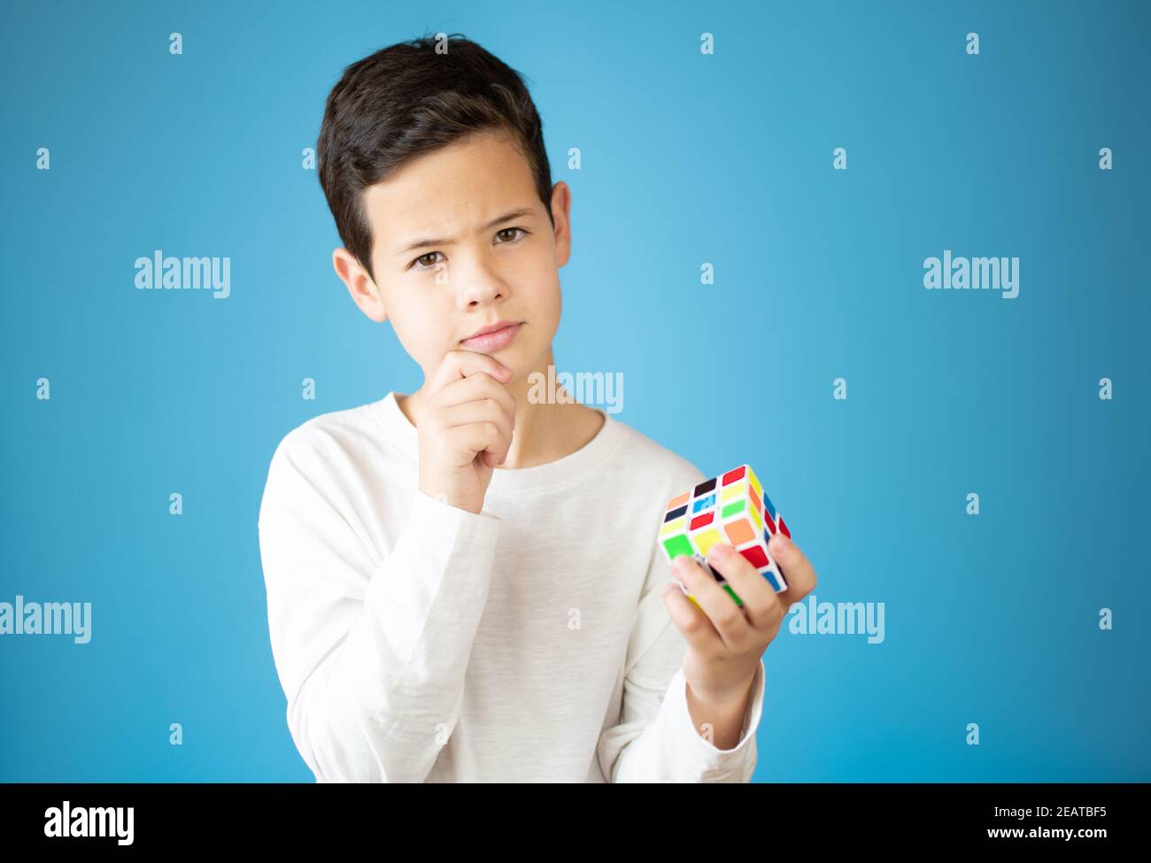Young boy pensive plays with rubik's cube over blue background Stock ...