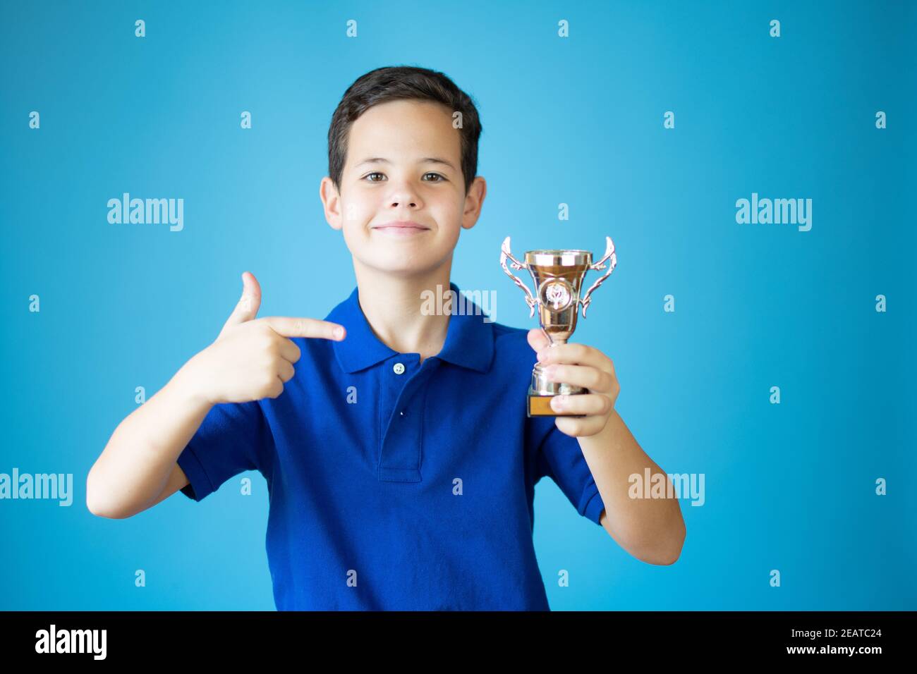 young boy holding a trophy with celebrating pose over blue background ...