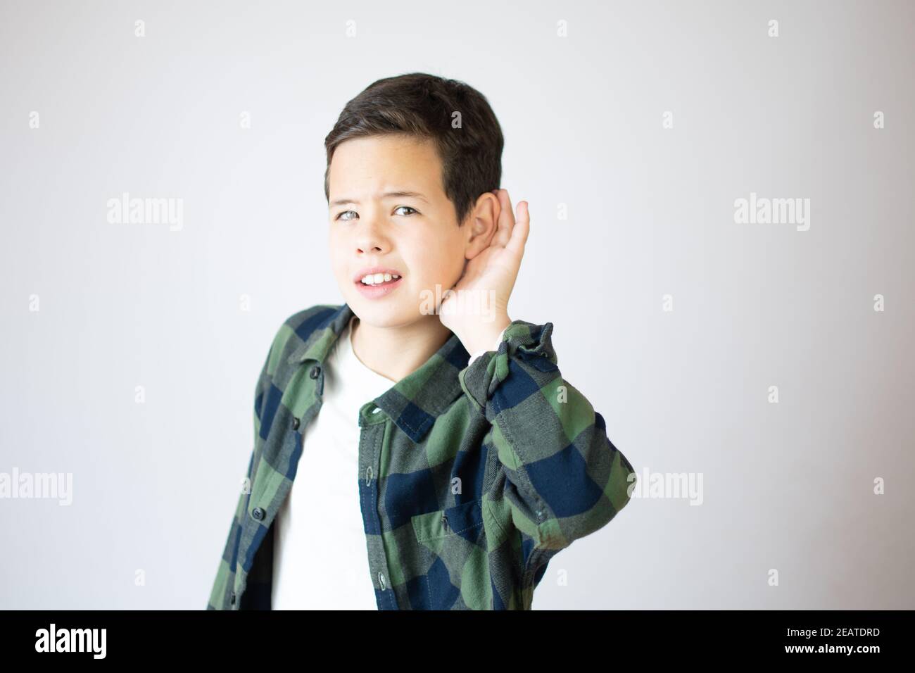 Concentrated young boy making a gesture of trying to hear something ...
