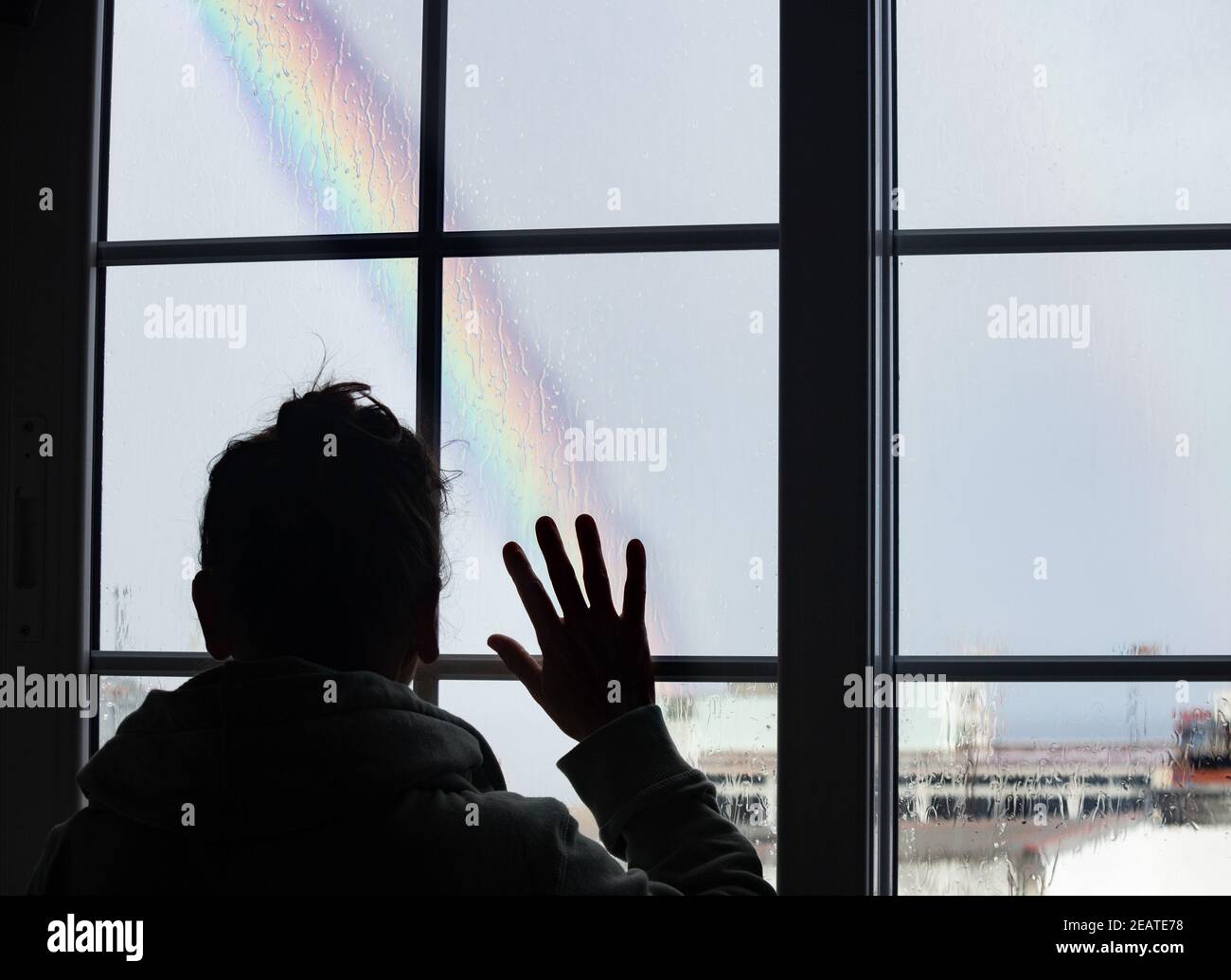 Woman looking out of window towards rainbow on rainy day. Conept image ...