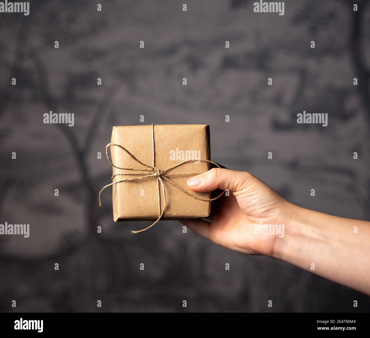 Hand holding a gift wrapped in brown craft paper on dark background ...