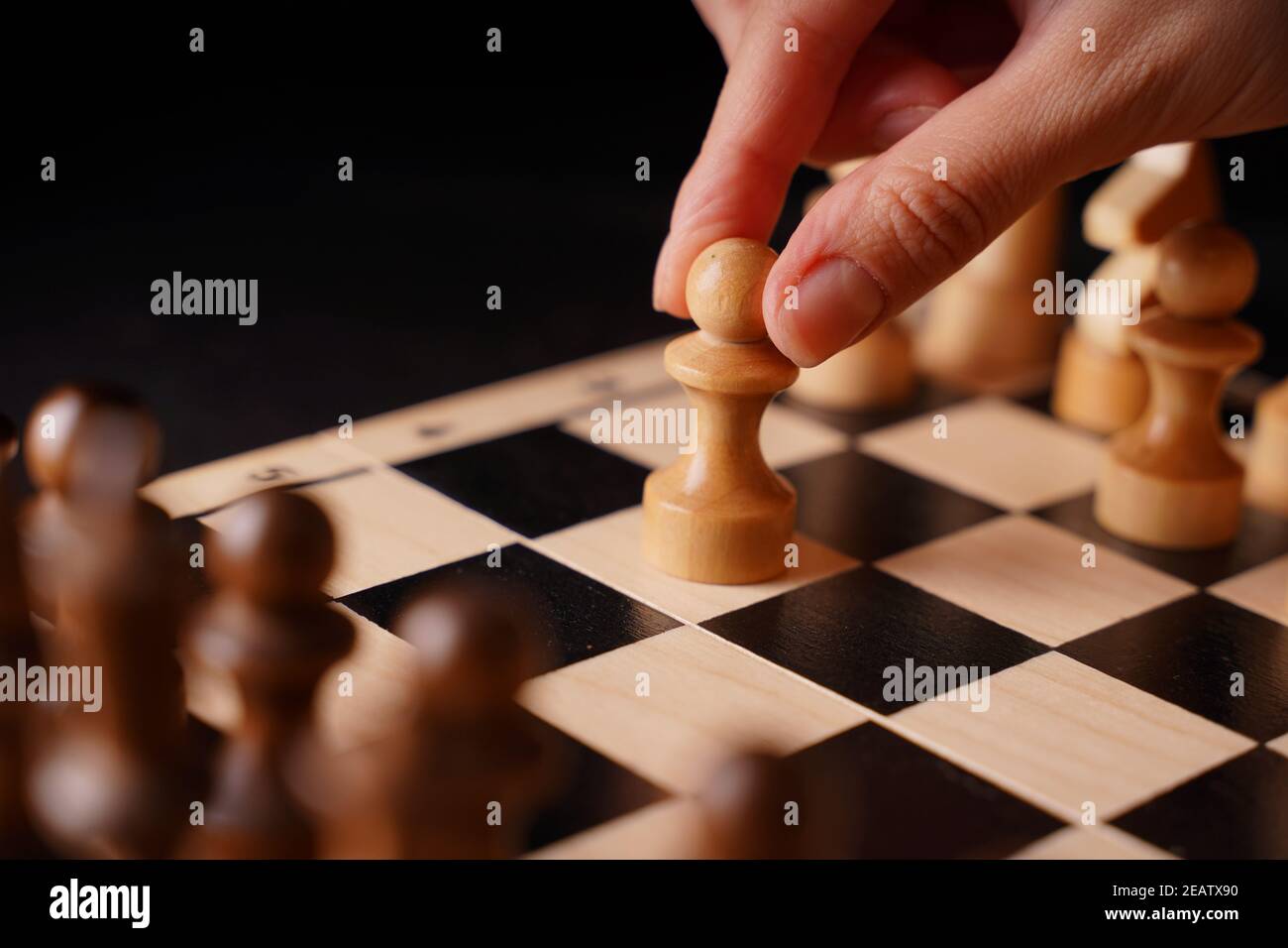 Close up of white and black wooden chess pieces on board. Woman's hand ...