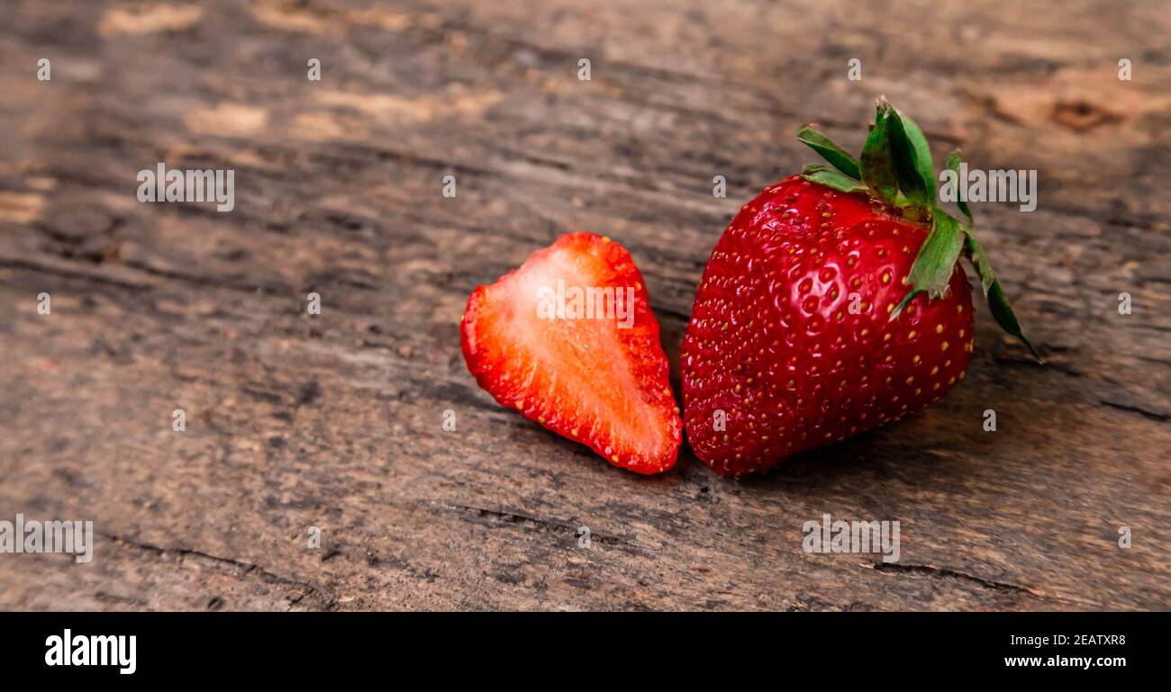 One whole strawberry and one half strawberry on a dark wooden surface ...