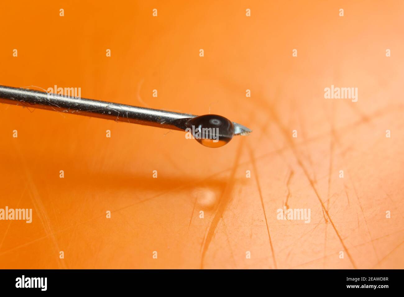 Water drop falling from the syringe needle against orange background ...