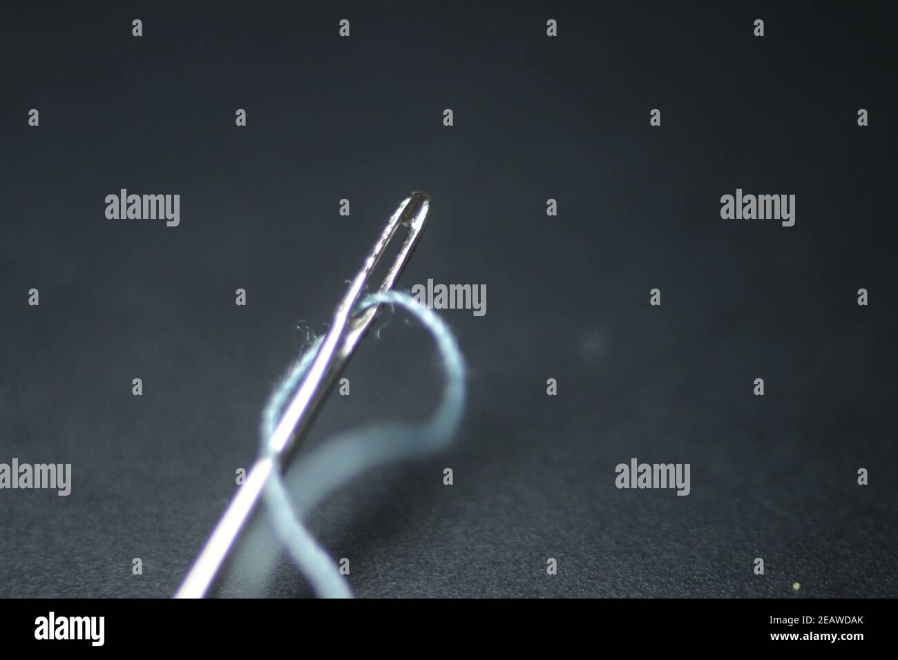 Small needle with thread in the eyelet, isolated over the black ...