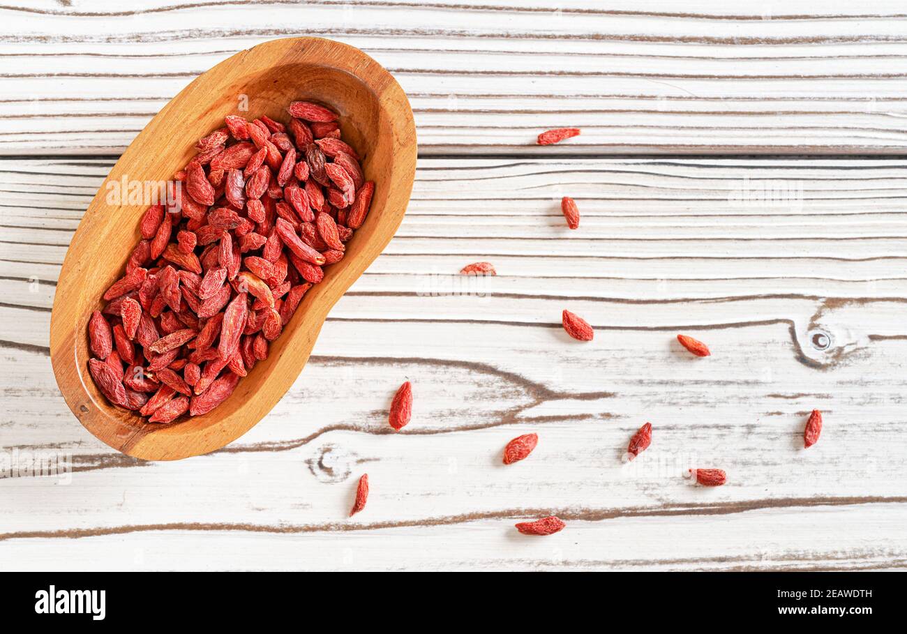 Dried goji aka. wolfberry seeds in wooden bowl and spilled on white ...