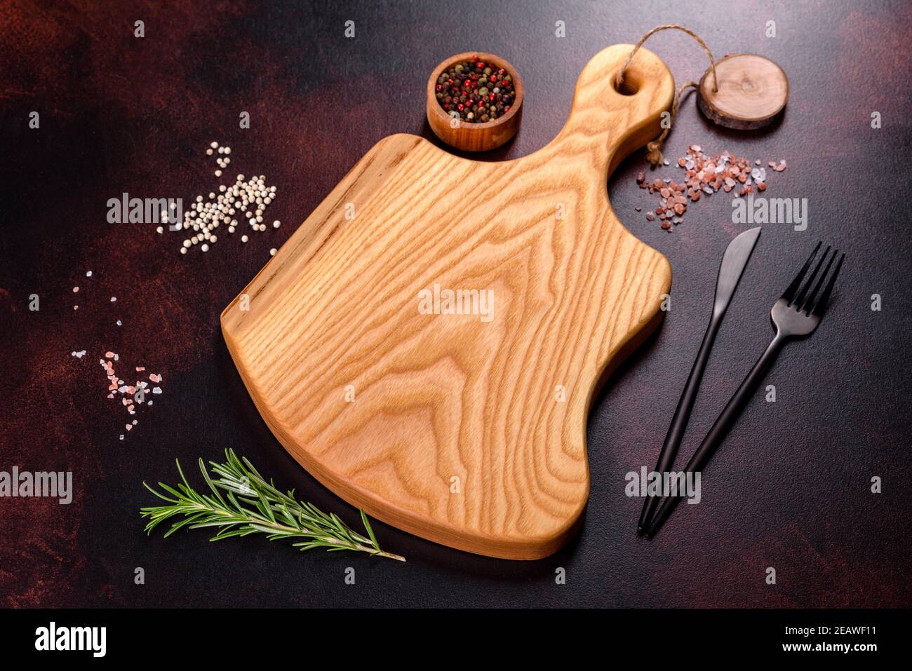 Cutting board with salt, spices and herbs on a dark concrete background ...
