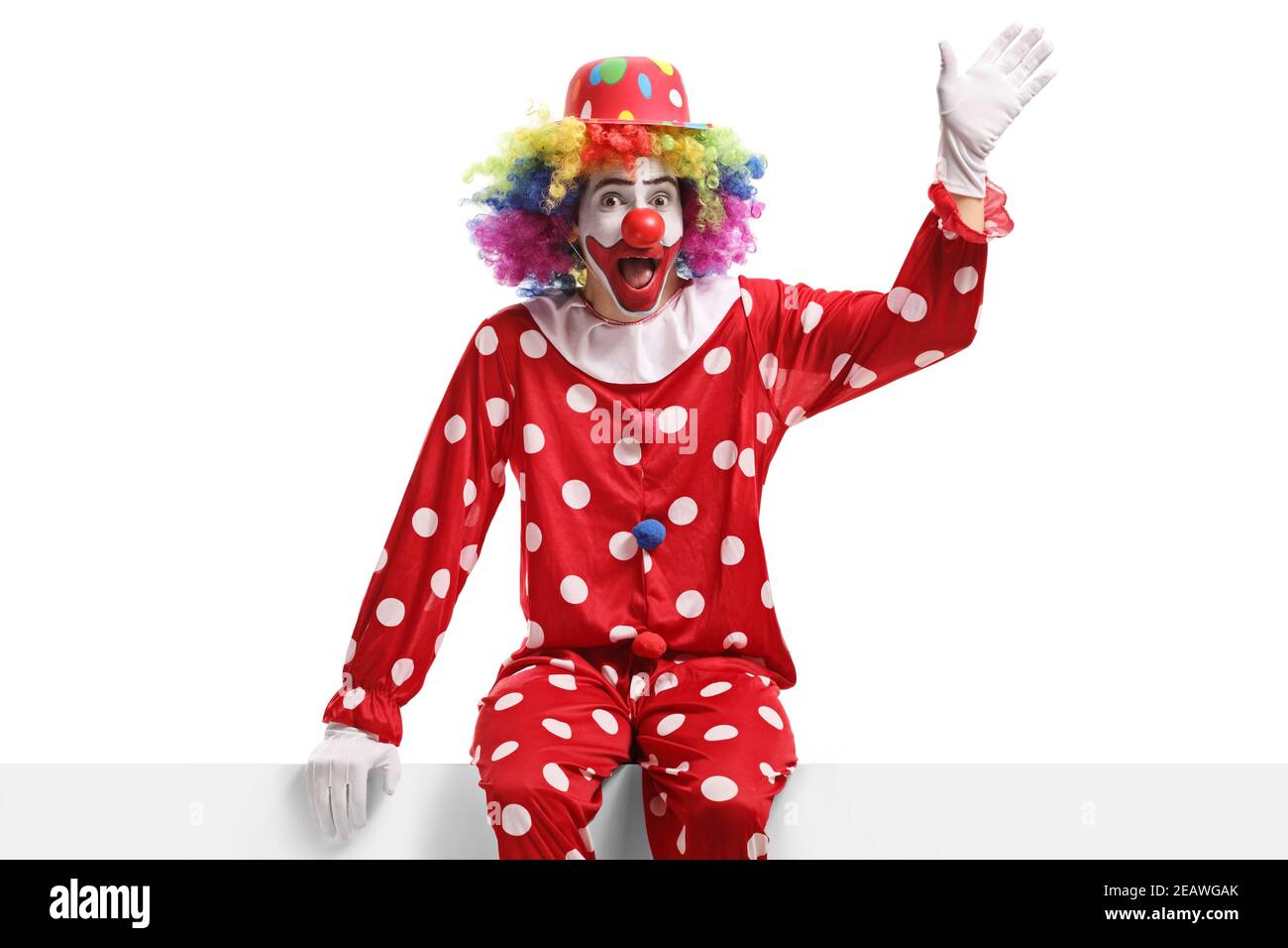 Clown sitting on a white panel and waving isolated on white background ...