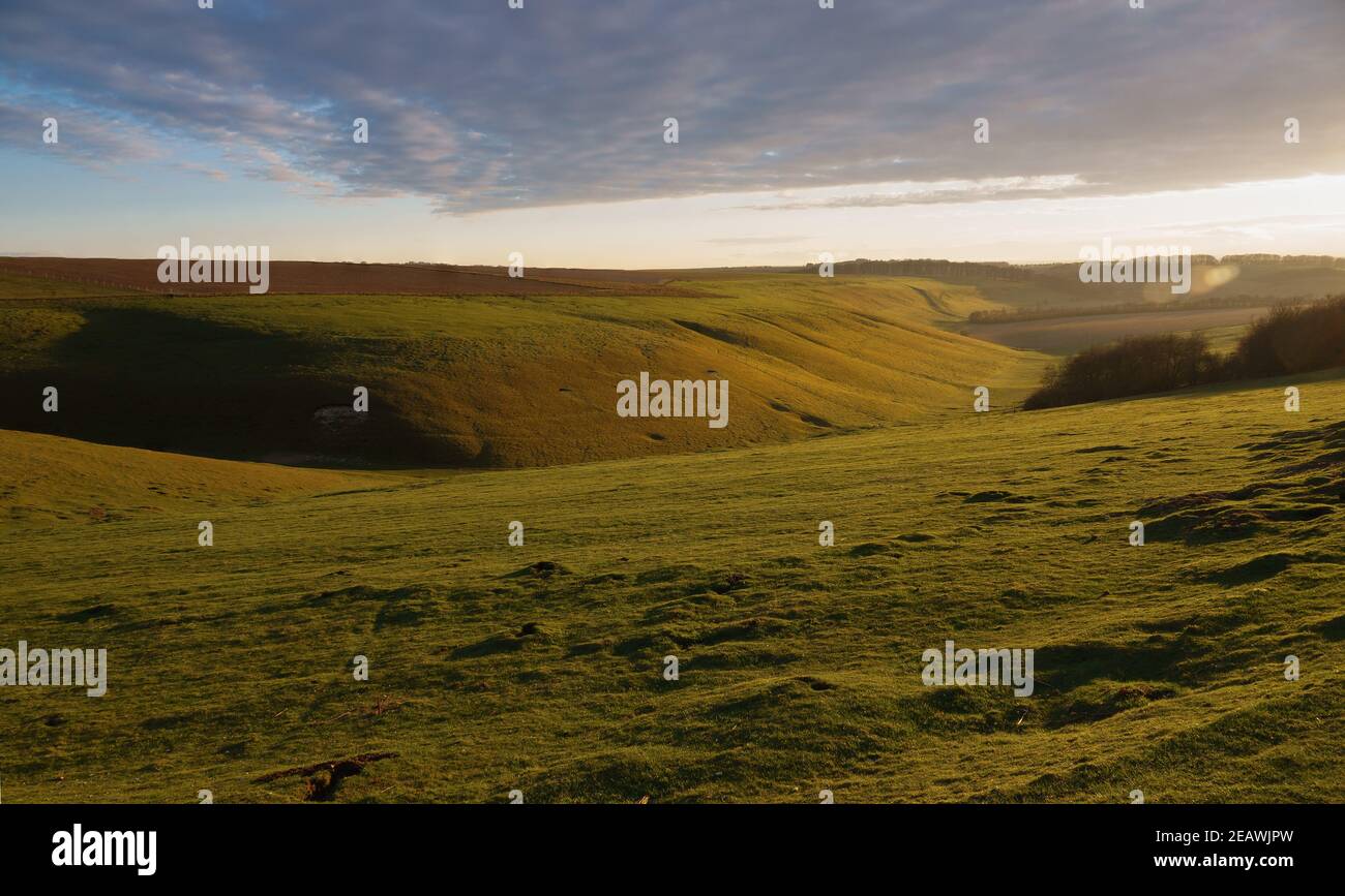 Sunset illuminates a deep English valley with grass fields glowing ...