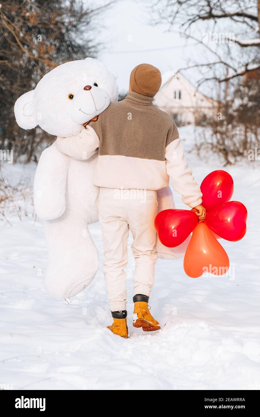 Young man from behind hugs holding big teddy bear soft toy gift heart ...