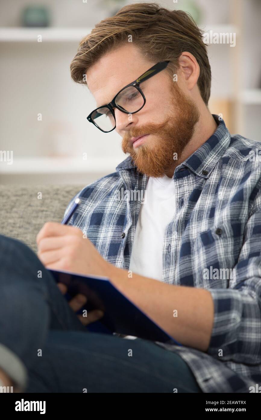 intelligent man writing in book sat on the sofa Stock Photo - Alamy