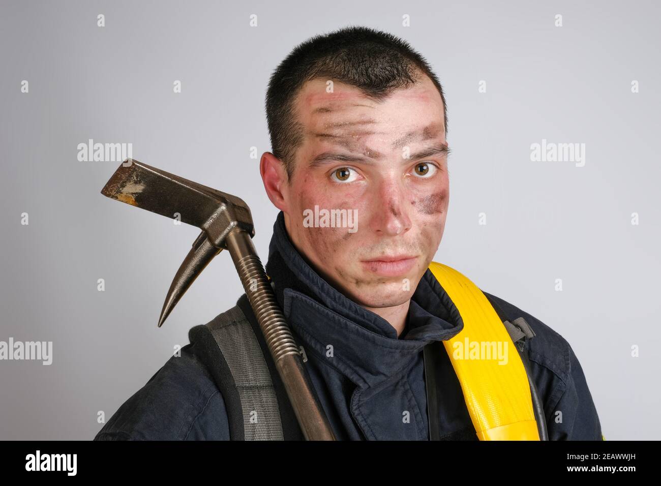 Close-up face of young brave man in uniform of firefighter and crowbar ...