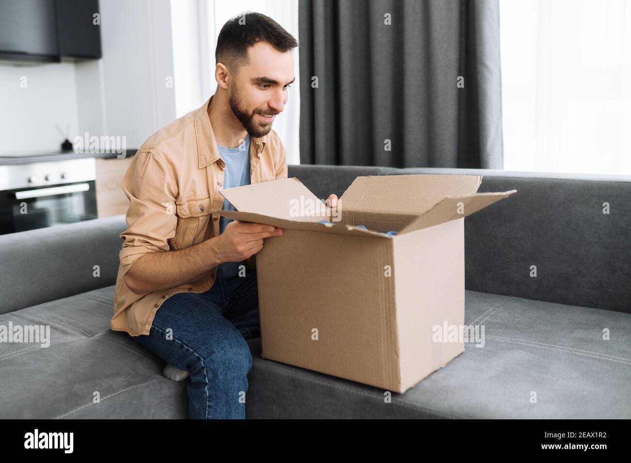Home delivery. Stylish caucasian guy got his order, unpack a parcel ...