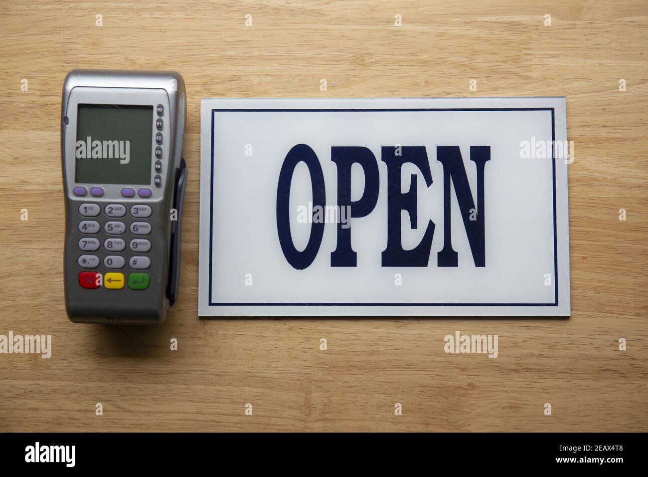 Card and cheque terminal and a sign "OPEN" on a wooden table ...