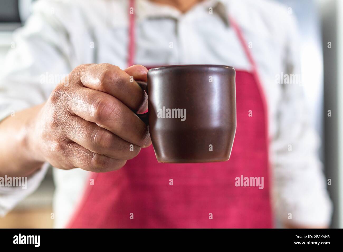 Close-up of a man's hand offering a cup of coffee. Barista in a coffee ...