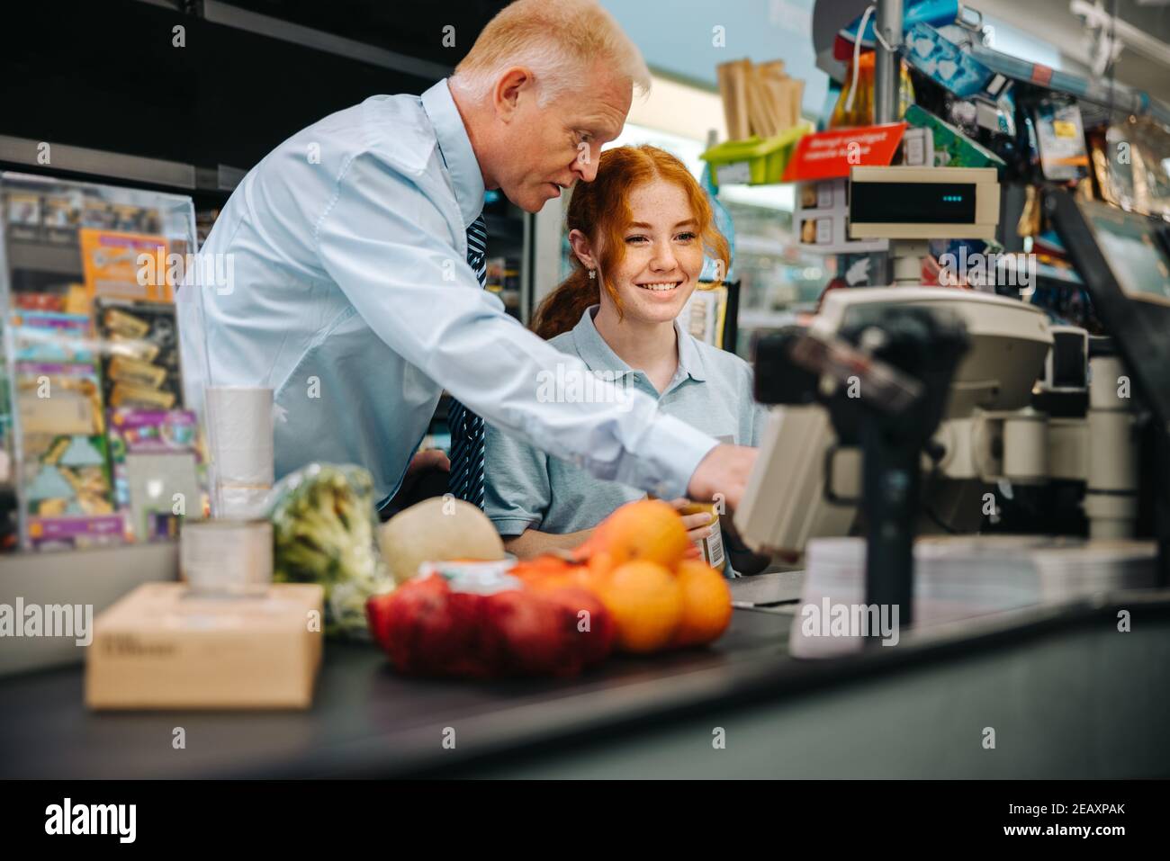 Senior manager giving training to a new female employee at checkout ...