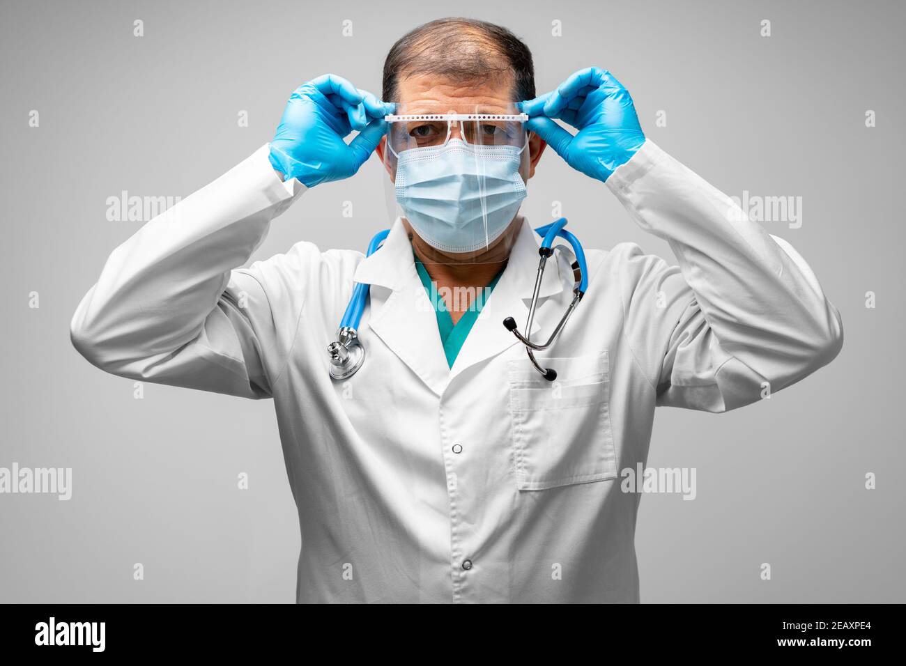 Middle-aged male doctor putting on face shield, grey background Stock ...