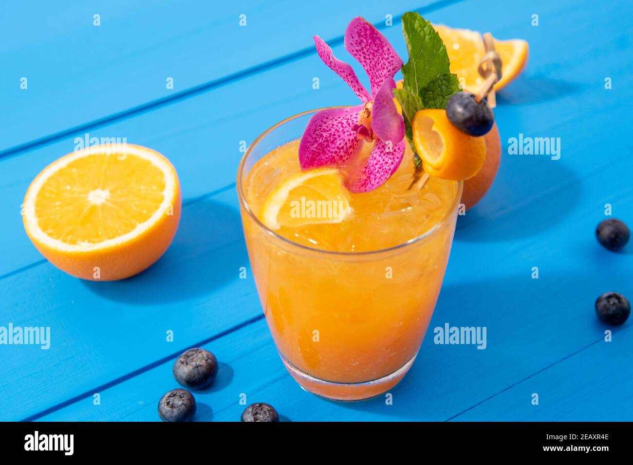 Iced summer orange refreshing drink being served on blue wooden table ...