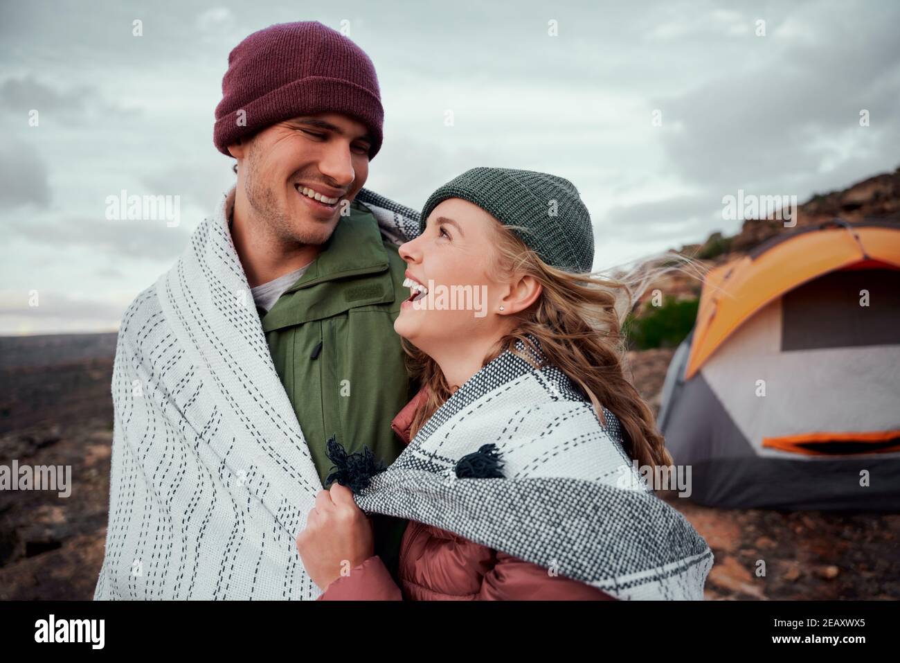 Laughing young romantic couple in a blanket standing together outside ...