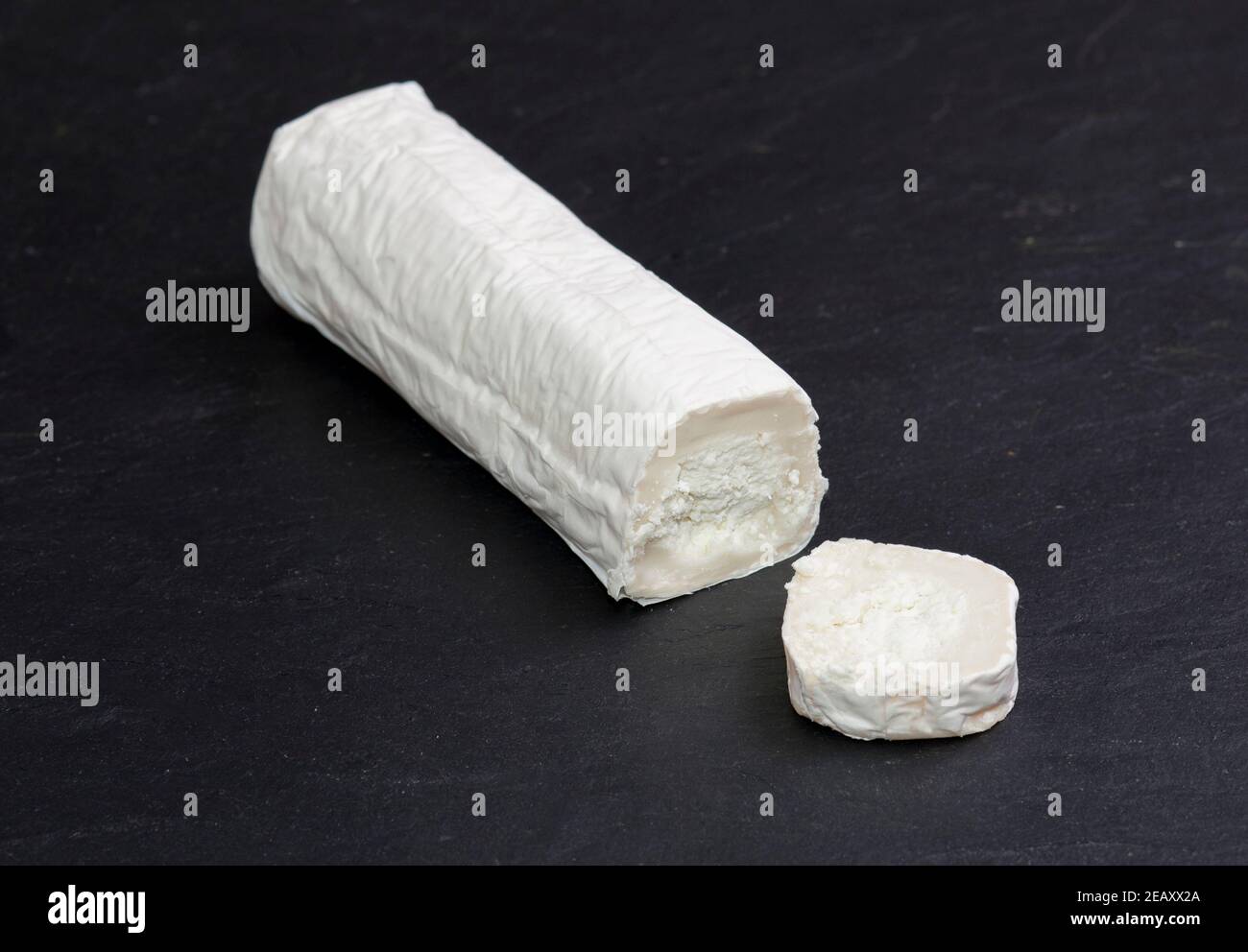 Goat cheese roller with slice. Isolated over black slate Stock Photo ...