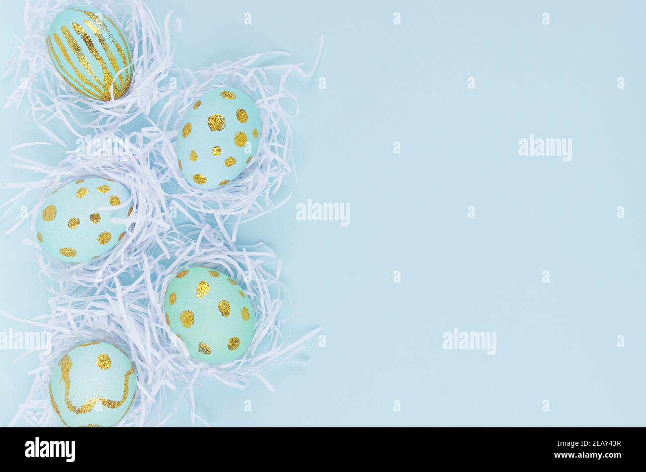 Handmade blue easter eggs with golden glitter design in white nest as ...