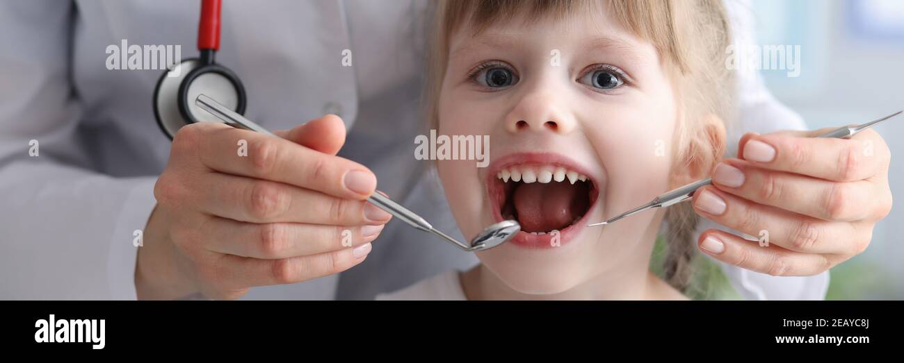 Dentist doctor with stethoscope examines teeth of little girl in clinic ...