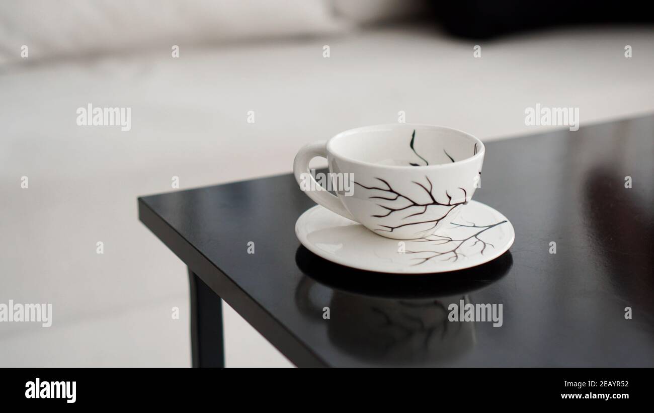 White coffee cup with a pattern of black branches on a black table ...