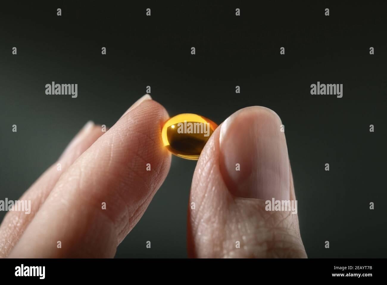 Female hand holding a small yellow capsule of nutritional supplement ...