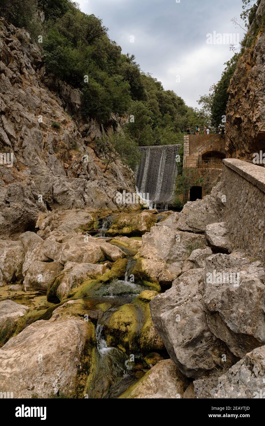 Vertical shot of high rocks covered with trees and a waterfall floating ...