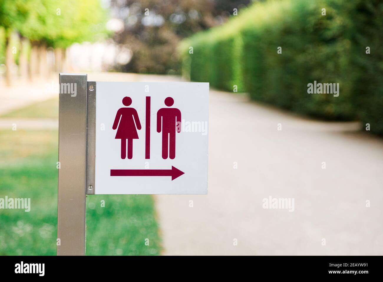 Signpost for men's and women's restrooms in park near trimmed tall ...