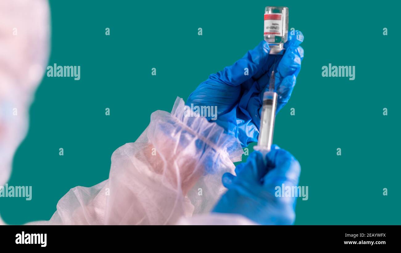 A doctor wearing a PPE suit holds a syringe and bottle with a vaccine ...
