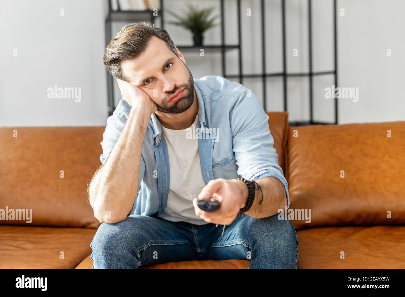 Handsome bored young man holding tv remote control, watching boring TV ...