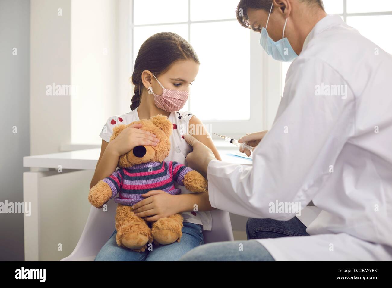 Brave child holding teddy and looking at needle while getting a shot at ...