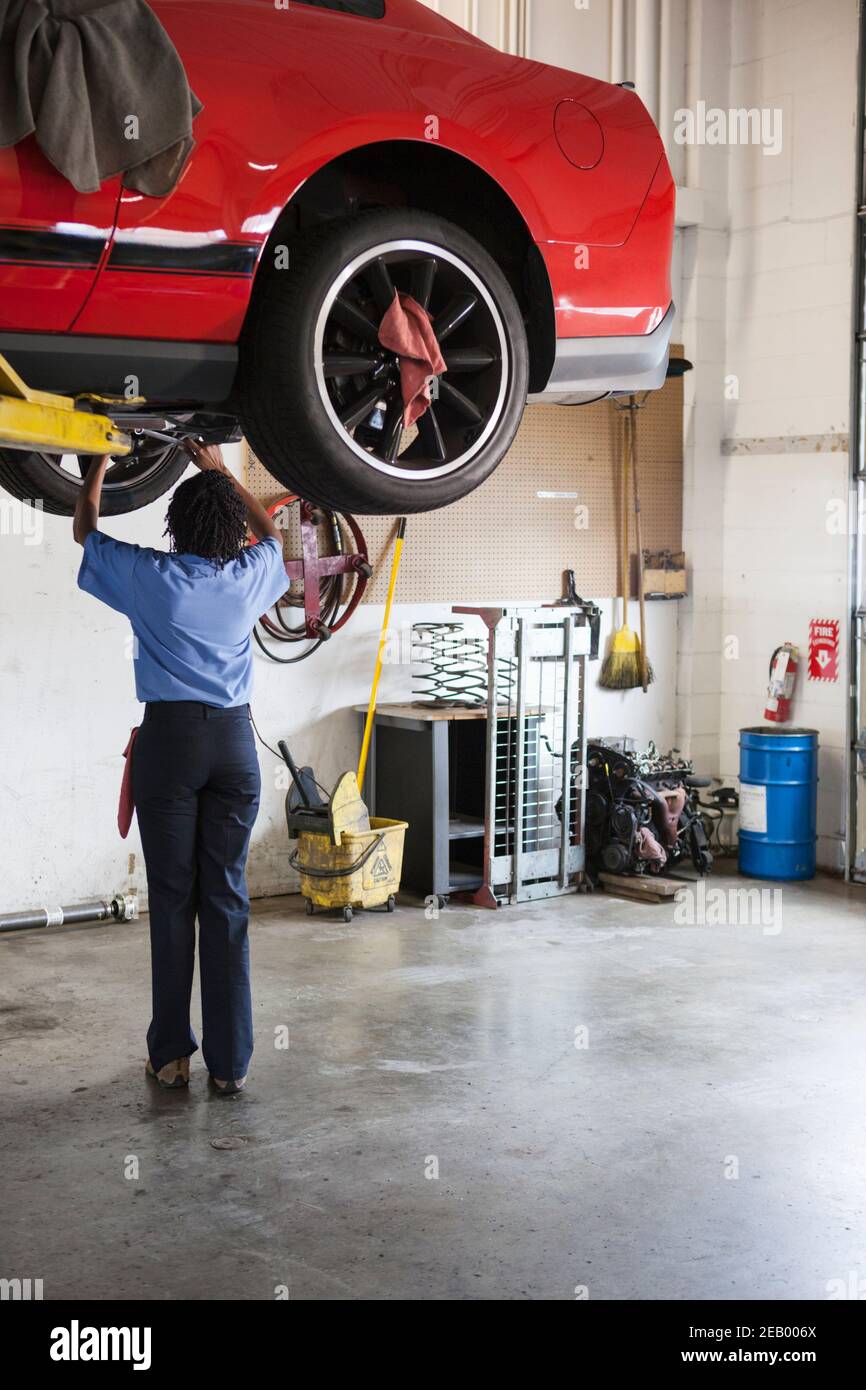 Mechanic in a repair shop works on the underside of a car up on a lift ...