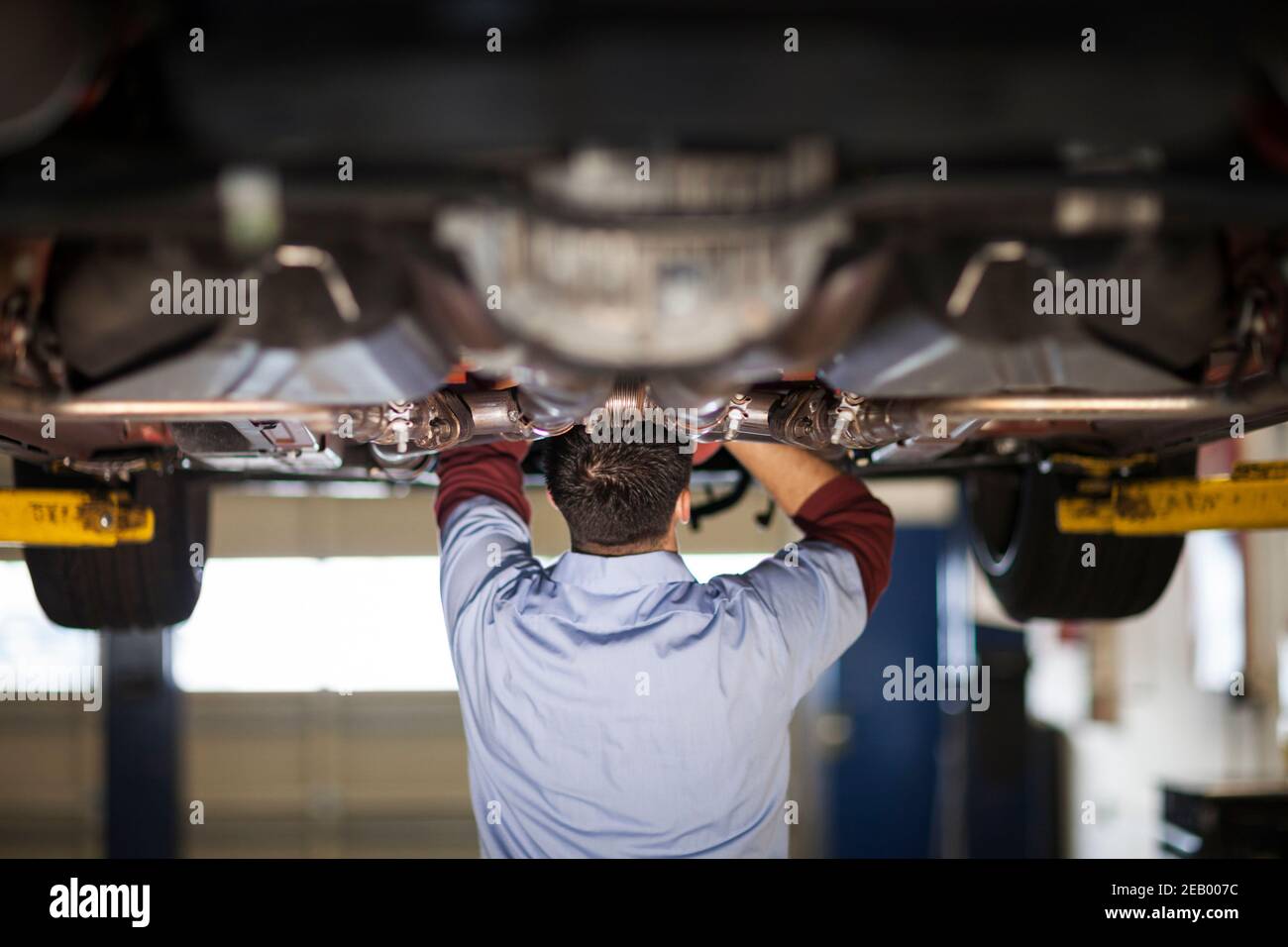 Mechanic in a repair shop works on the underside of a car up on a lift ...
