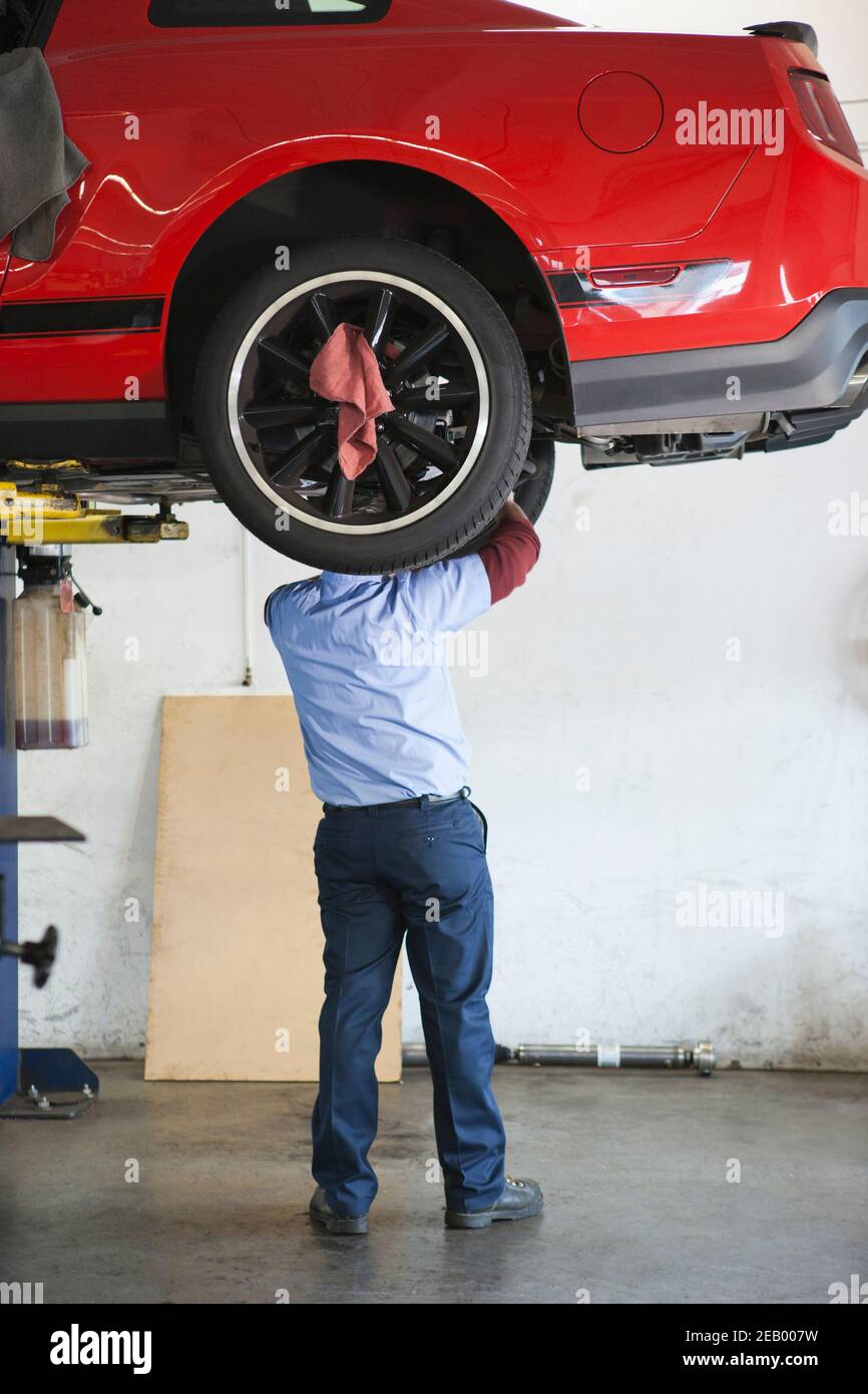 Mechanic in a repair shop works on the underside of a car up on a lift ...