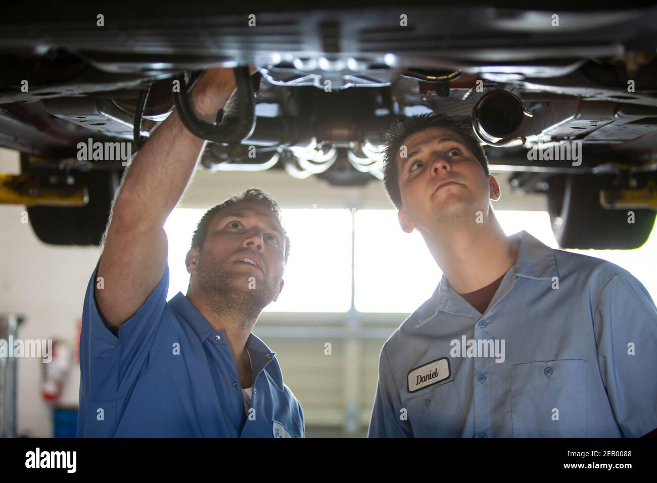 Two mechanics work on the underside of a car on a lift in a repair shop ...