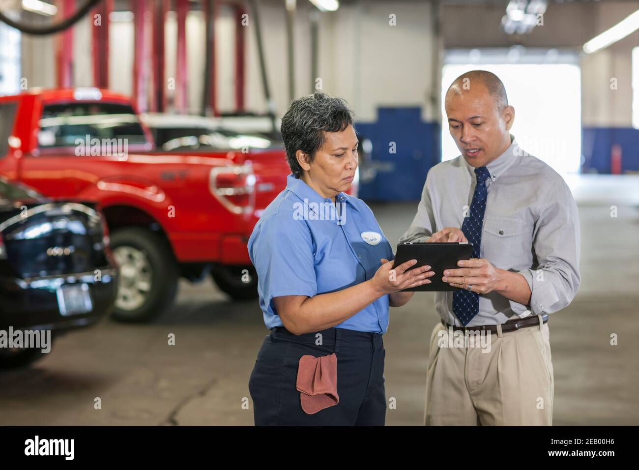 Male Pacific Islander auto repair shop manager talks to female Hispanic ...