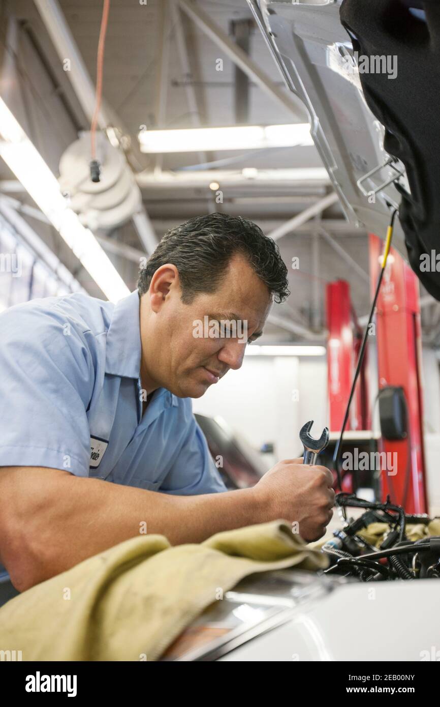 Hispanic mechanic leans into an engine of a car he is working on in an ...