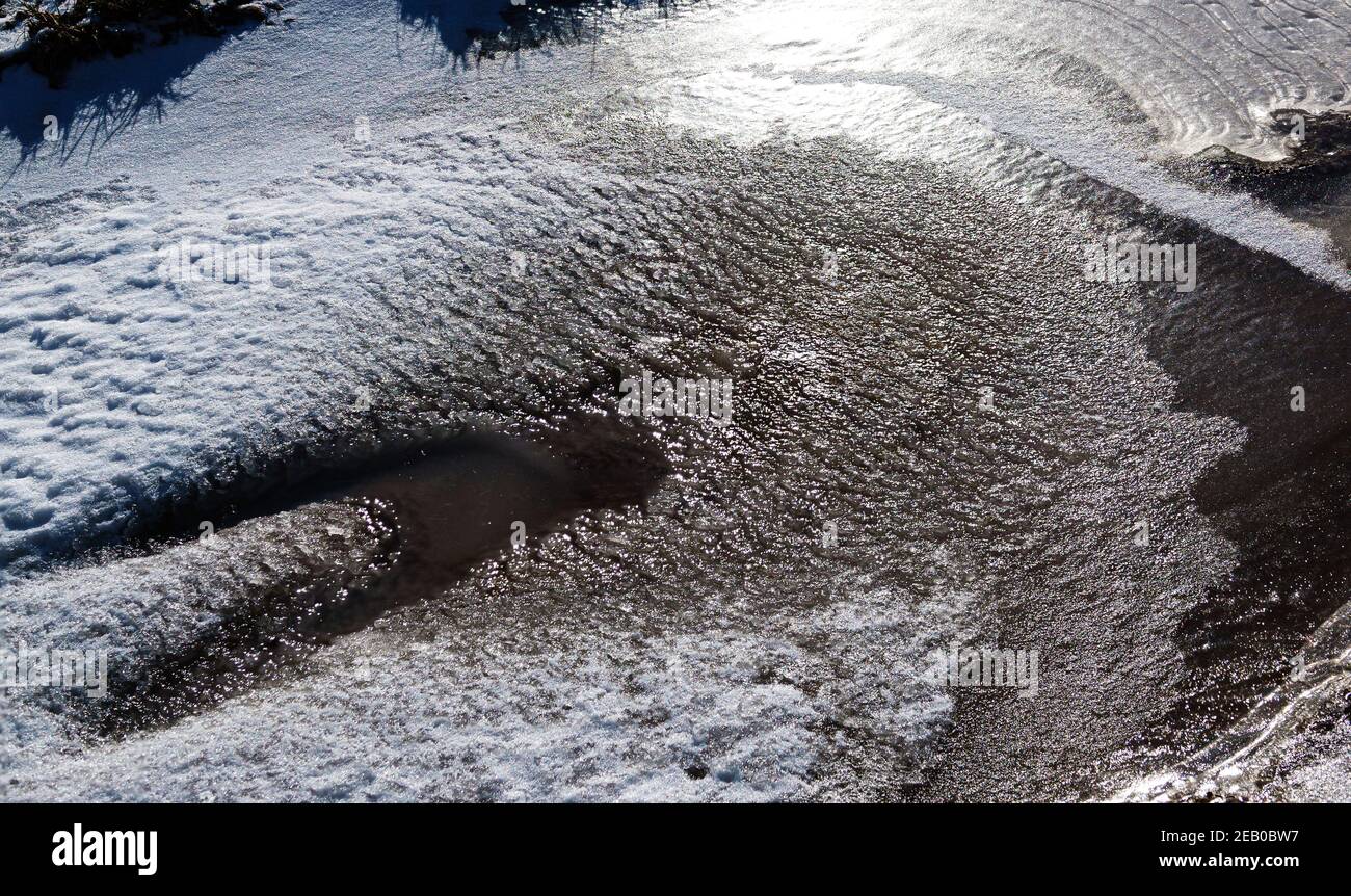 snow covered frozen puddle with patterns from the strong winds as the ...