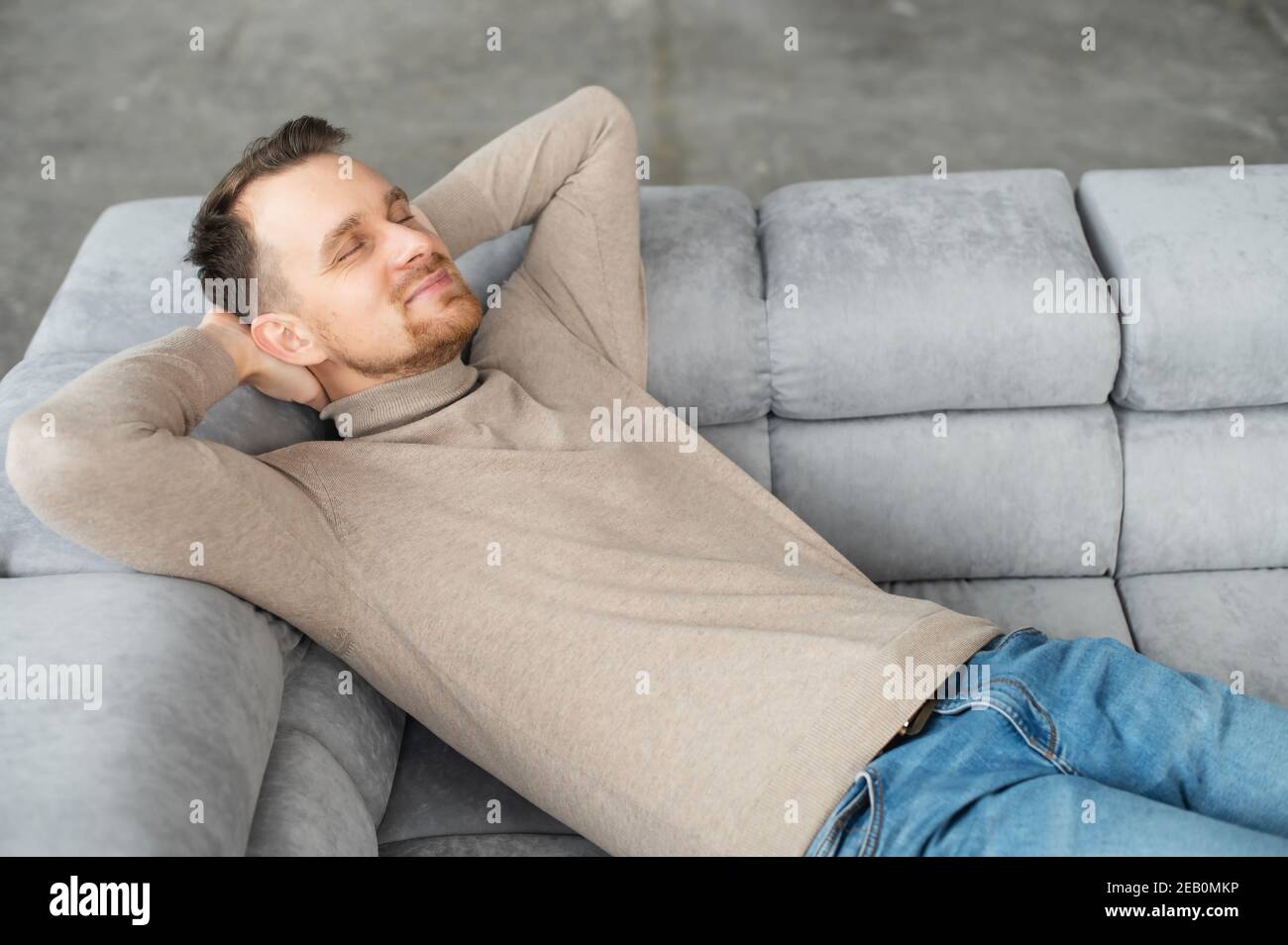 Handsome smiling guy take a nap lying on the comfortable sofa with eyes ...