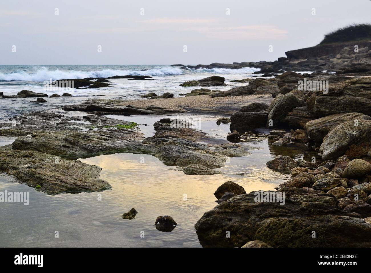 Big rocks on the beach. Waves in the ocean. Sunset sky reflected in ...