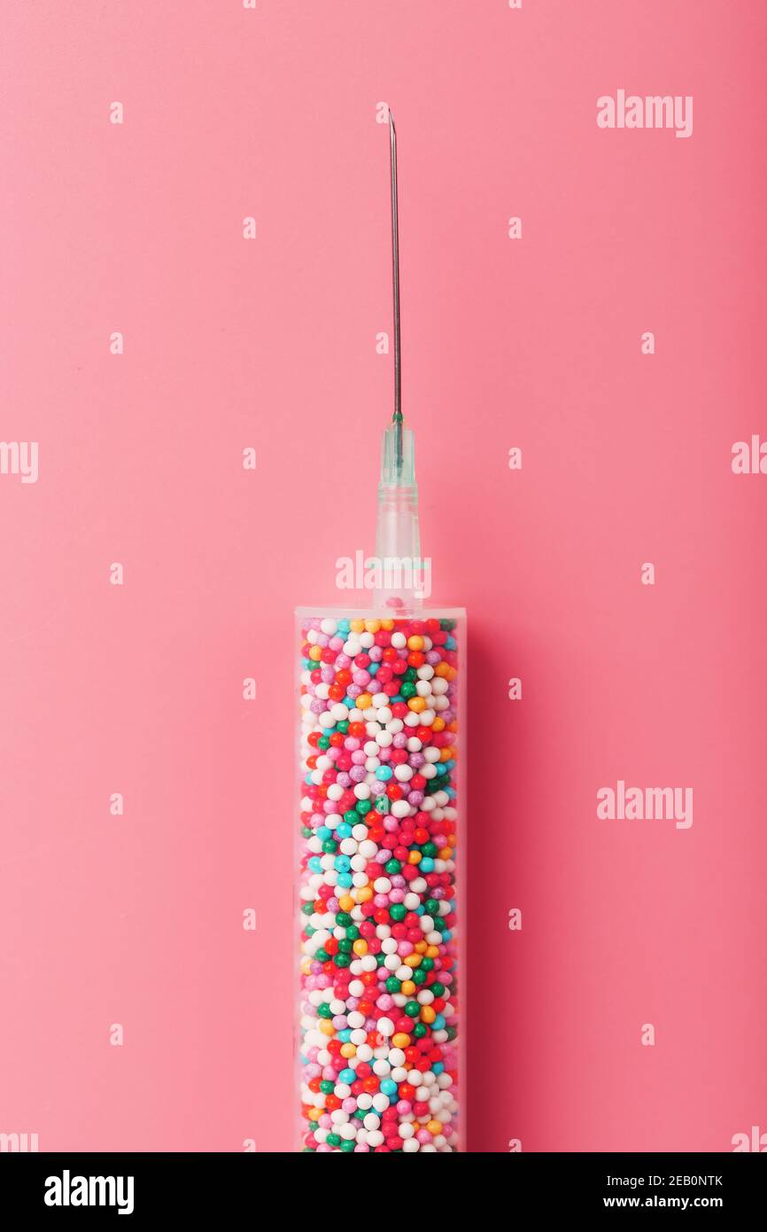Medical Syringe filled with colorful balloons on a pink background with ...