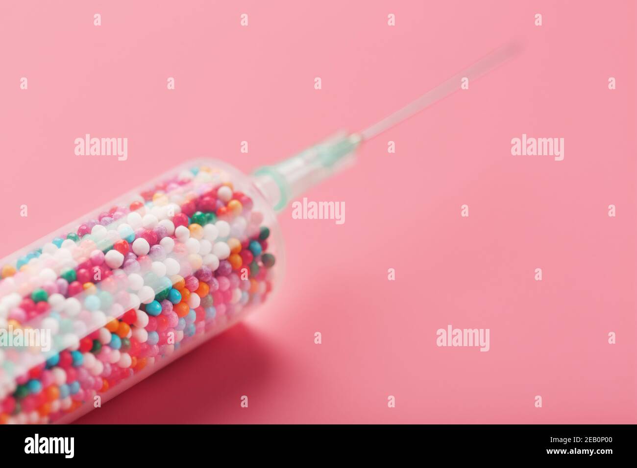 Medical Syringe filled with colorful balloons on a pink background with ...
