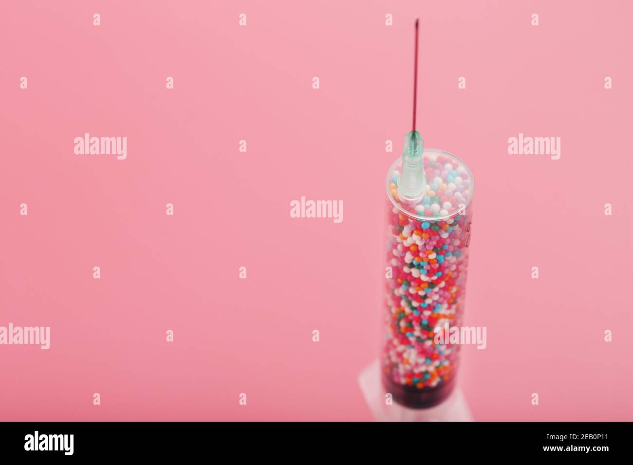 Medical Syringe filled with colorful balloons on a pink background with ...