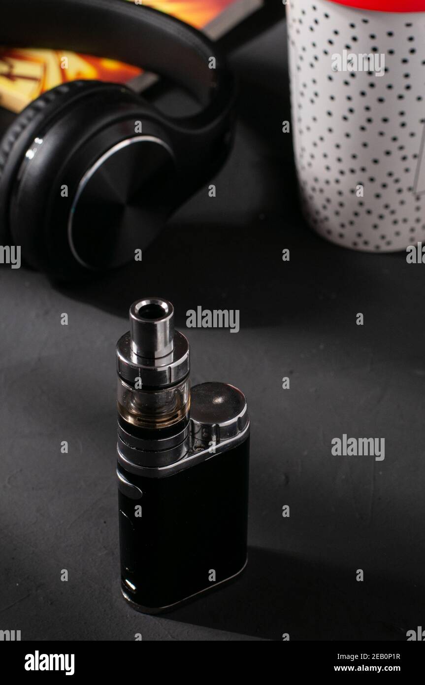 Refillable vape pod, headphones, and a plastic coffee cup on the dark ...