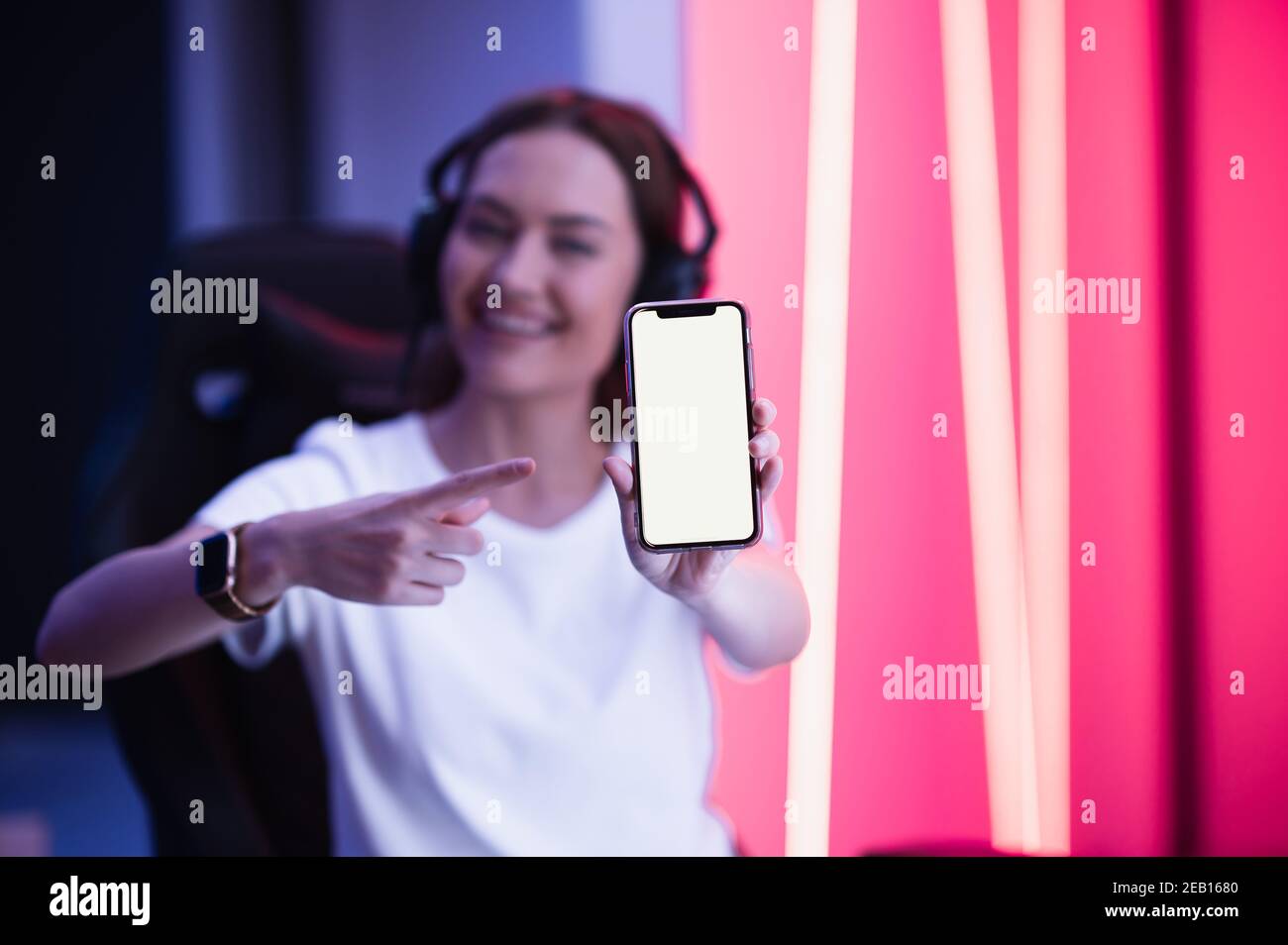Cheerful gamer girl pointing with finger at smartphone with blank ...